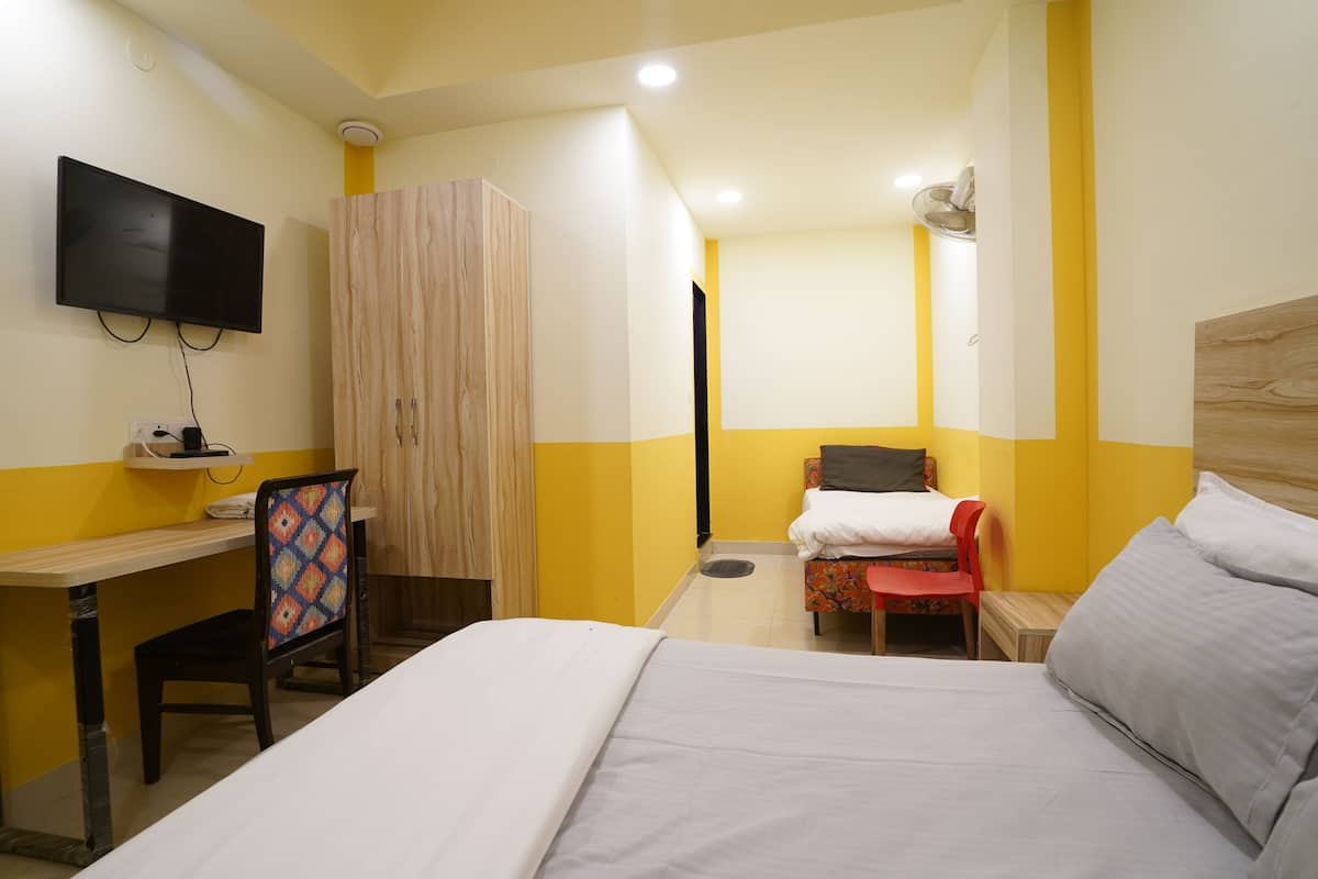 Quarto de hotel com cama, escrivaninha, cadeira, televisão e guarda-roupa.