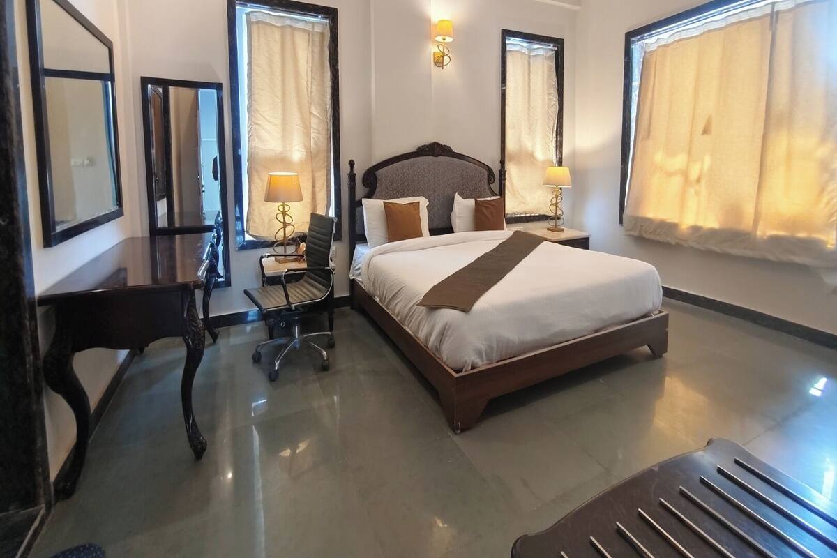 Quarto de hotel com uma cama grande, uma escrivaninha, uma cadeira e duas luminárias de cabeceira.
