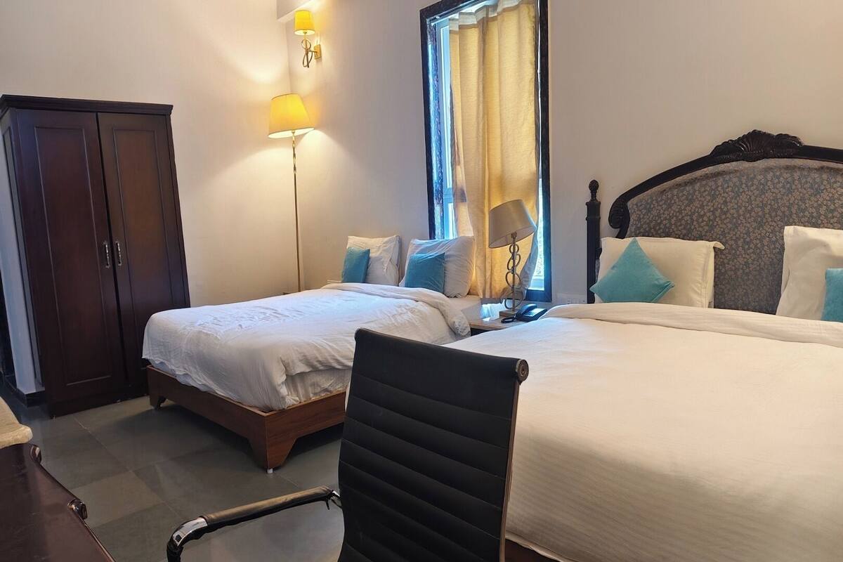 Quarto de hotel com duas camas, um guarda-roupa, uma cadeira e uma janela com cortinas.