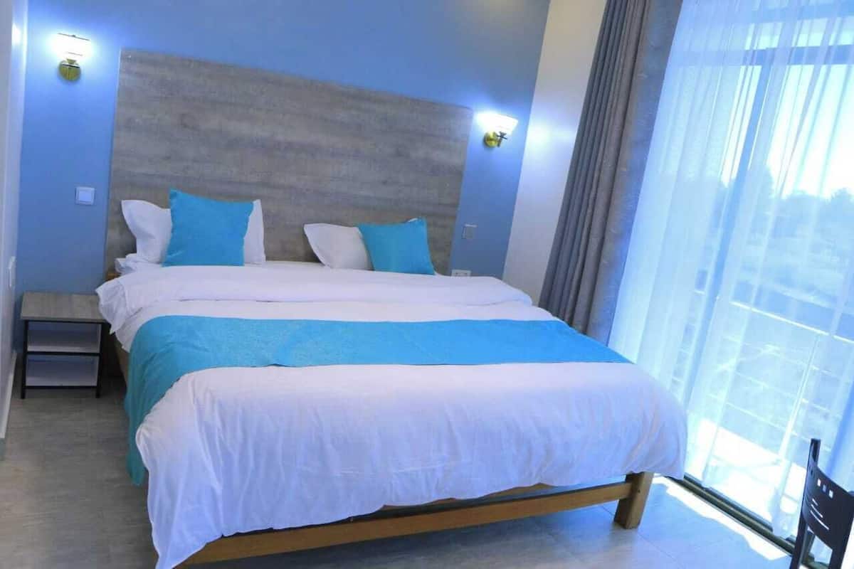 Uma cama de casal com estrutura de madeira, duas mesas de cabeceira e uma janela grande com cortinas.