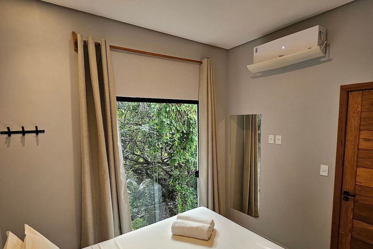 Quarto com cama, janela com cortinas, luminária no teto e ar-condicionado.