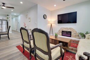 Uma sala de estar moderna com lareira, uma TV fixada na parede e um espaço de jantar com cadeiras e mesa.