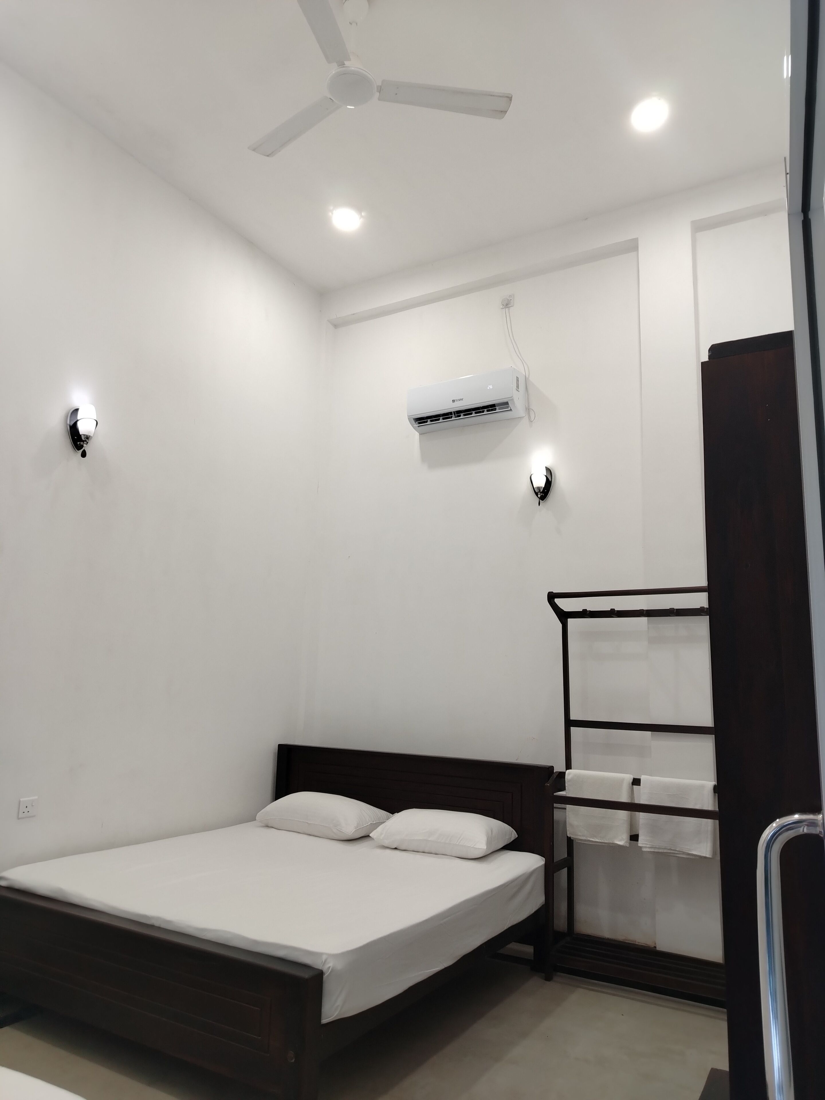 Quarto com cama, ventilador de teto, ar-condicionado e prateleira na parede.