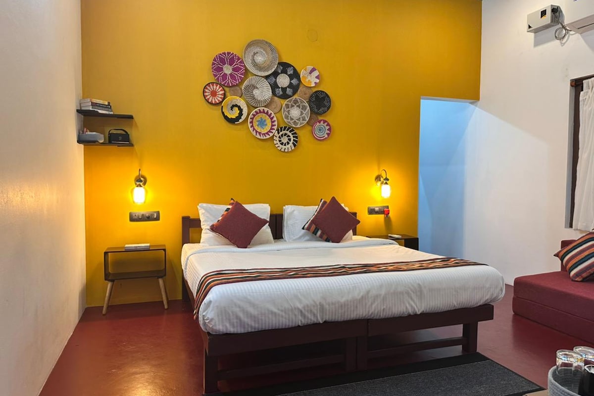 Quarto com cama, mesas de cabeceira, luminária na parede e sofá vermelho.