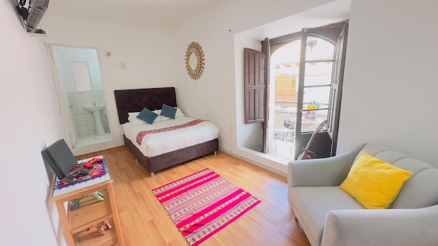Quarto com cama, sofá, janela e uma pequena mesa com um laptop.