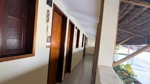 Corredor com portas de madeira, piso ladrilhado e vista para o exterior por uma janela.