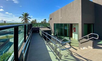 Um edifício moderno com fachada de vidro, escadas externas e vista clara para palmeiras e vegetação ao fundo.