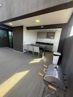Uma cozinha ao ar livre moderna com mesa e cadeiras, churrasqueira e lixeira.