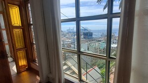 Quarto com uma janela grande que dá para uma vista urbana com edifícios e guindastes.