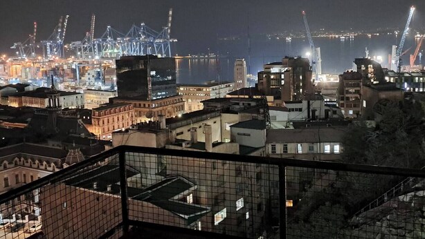 Vista noturna de uma paisagem urbana com edifícios e guindastes à beira-mar.