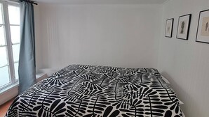 Quarto com cama, janela com cortinas e três quadros na parede.