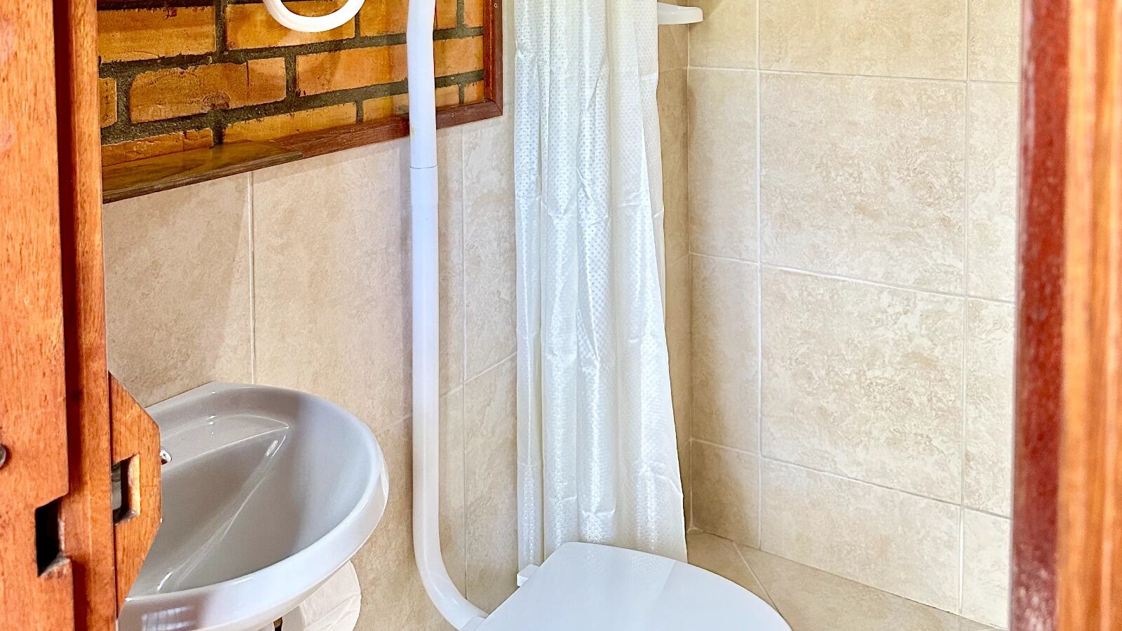 Casa de banho com lavatório branco, cortina de chuveiro e paredes em azulejo.