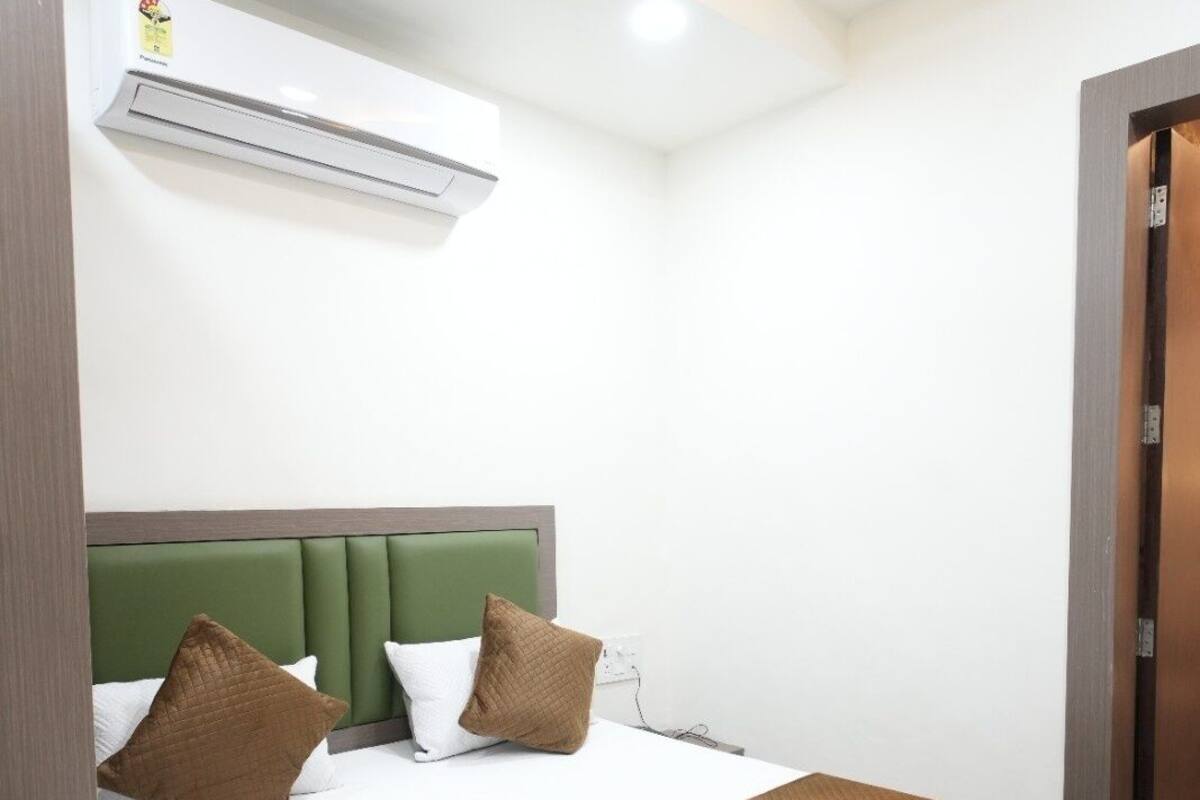 Quarto de hotel com cama, cabeceira verde, colcha acolchoada marrom e parede branca.