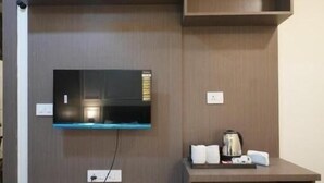 Quarto moderno com televisão de tela plana presa a uma parede de madeira, uma escrivaninha com chaleira e uma lixeira.
