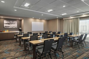 Sala de conferências com mesas, cadeiras, quadro branco e tela de projeção.