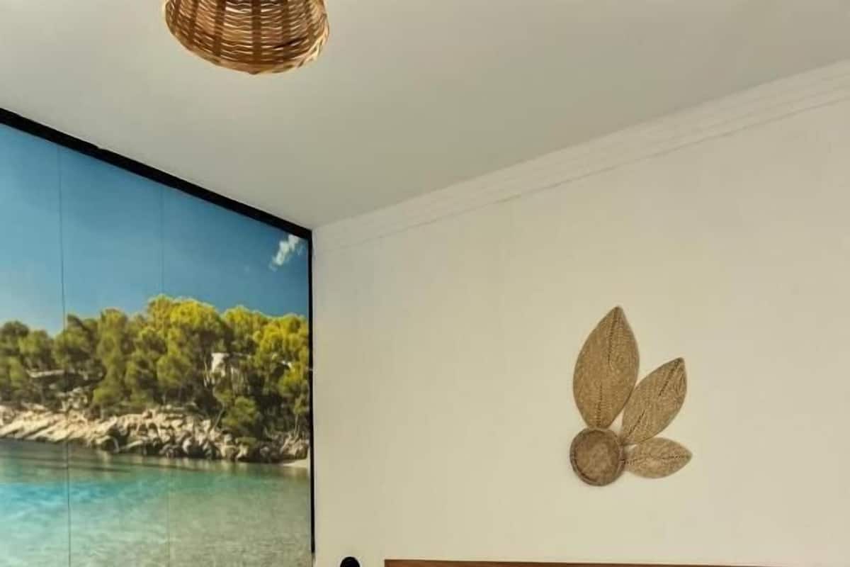 Quarto de hotel com uma janela ampla que oferece uma vista panorâmica da paisagem costeira, uma cama com roupa branca e uma peça decorativa na parede.