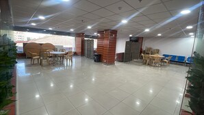 Um hall amplo com chão em mosaico, várias áreas de estar e uma grande janela com vista para o exterior.