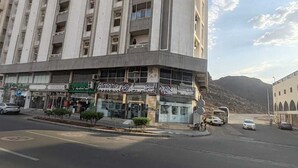 Um edifício de vários andares com fachada plana, vários espaços comerciais no térreo e uma área de estacionamento em frente.