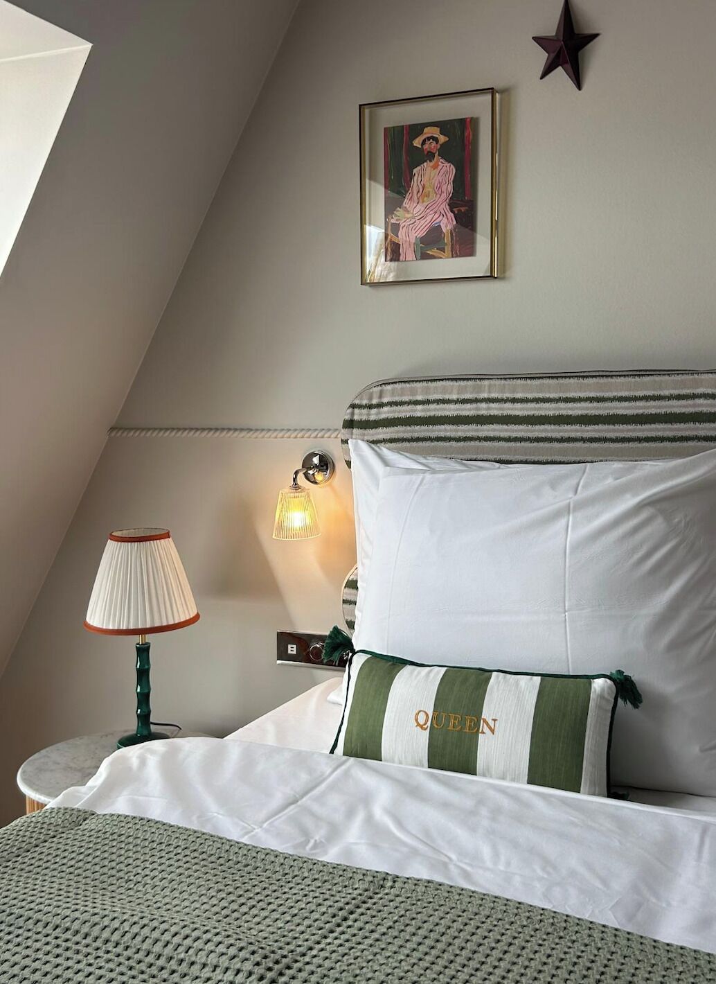 Quarto com cama, luminária, luz embutida na parede, quadro e decoração em forma de estrela.
