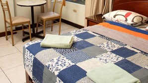 Quarto de hotel com cama, uma mesa pequena, duas cadeiras e uma janela com cortinas.