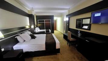Quarto de hotel com uma cama grande, escrivaninha, cadeira, televisão e guarda-roupa.