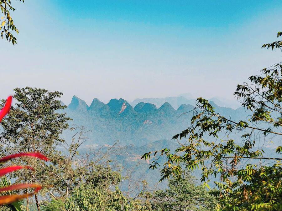 Paisagem montanhosa com vegetação densa em primeiro plano e céu claro.