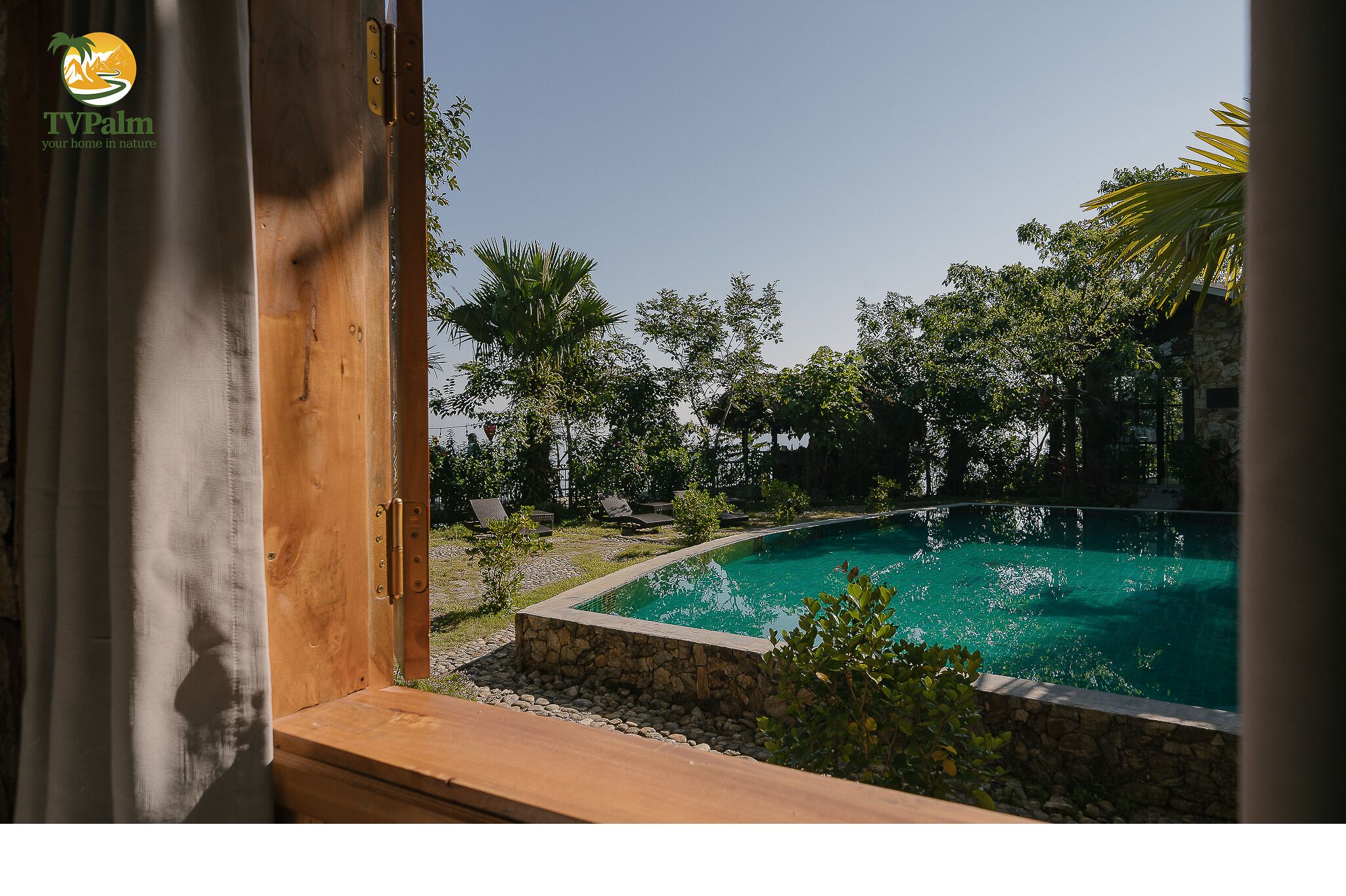 Vista de uma piscina rodeada de vegetação, com um deck de madeira e paredes de pedra.