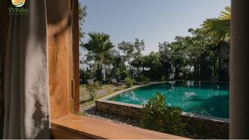 Vista de uma piscina rodeada de vegetação, com um deck de madeira e paredes de pedra.