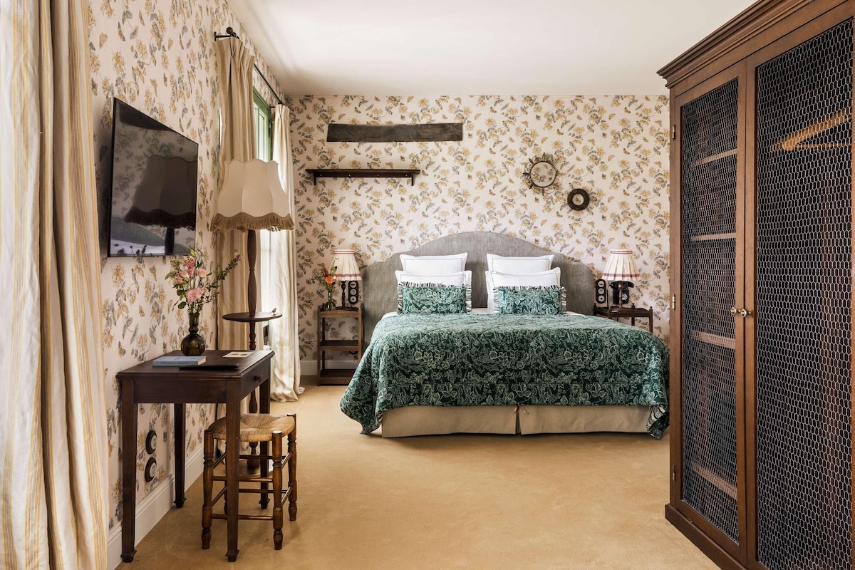 Quarto com cama, mesas de cabeceira, escrivaninha, cadeira, guarda-roupa e televisão.
