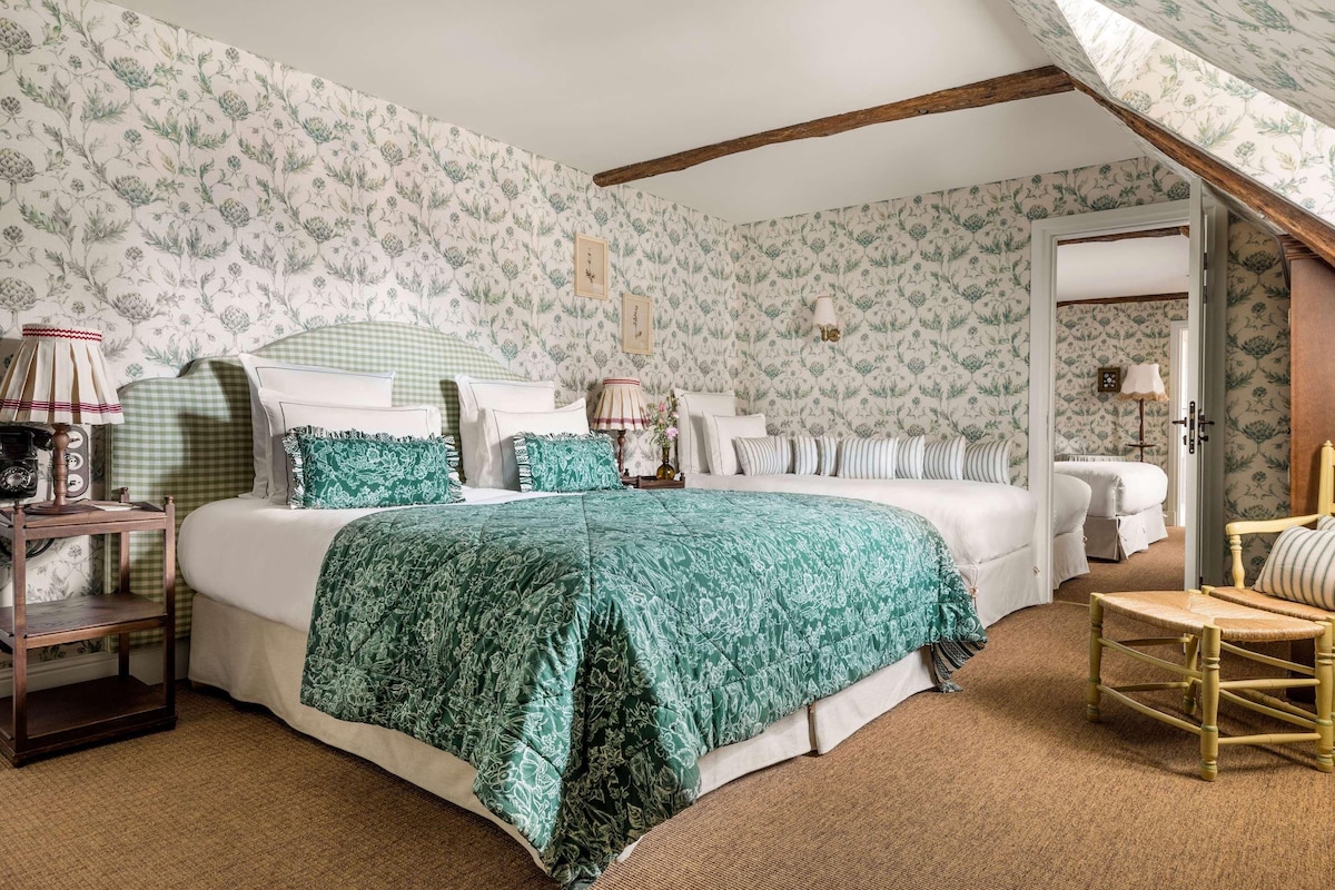 Quarto com uma cama grande, uma cadeira de madeira, uma mesa de cabeceira e um abajur.