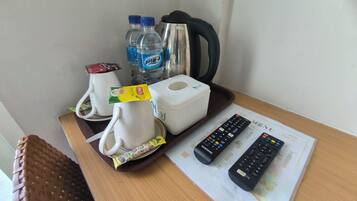 Uma bandeja com chaleira, duas garrafas de água, cafeteira, caixa de lenços de papel e dois controles remotos sobre uma mesa.