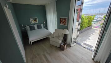 Quarto com cama, uma cadeira, luminária e vista para uma marina através de uma grande janela.
