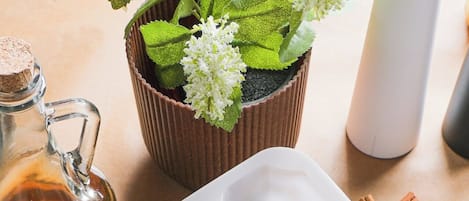 Uma bandeja de refeição com diversos alimentos, um jarro de vidro, uma planta em vaso e uma garrafa térmica.