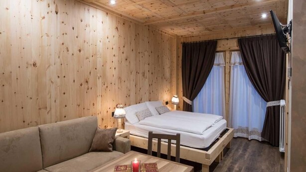 Quarto com painéis de madeira, uma cama, um sofá, uma mesa com uma vela e duas luminárias de cabeceira.