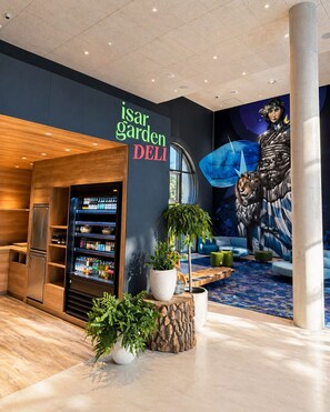 Decoração moderna com uma loja de delicatessen chamada 'Isar Garden Deli', uma máquina de vendas automática e um mural com a figura de um leão.