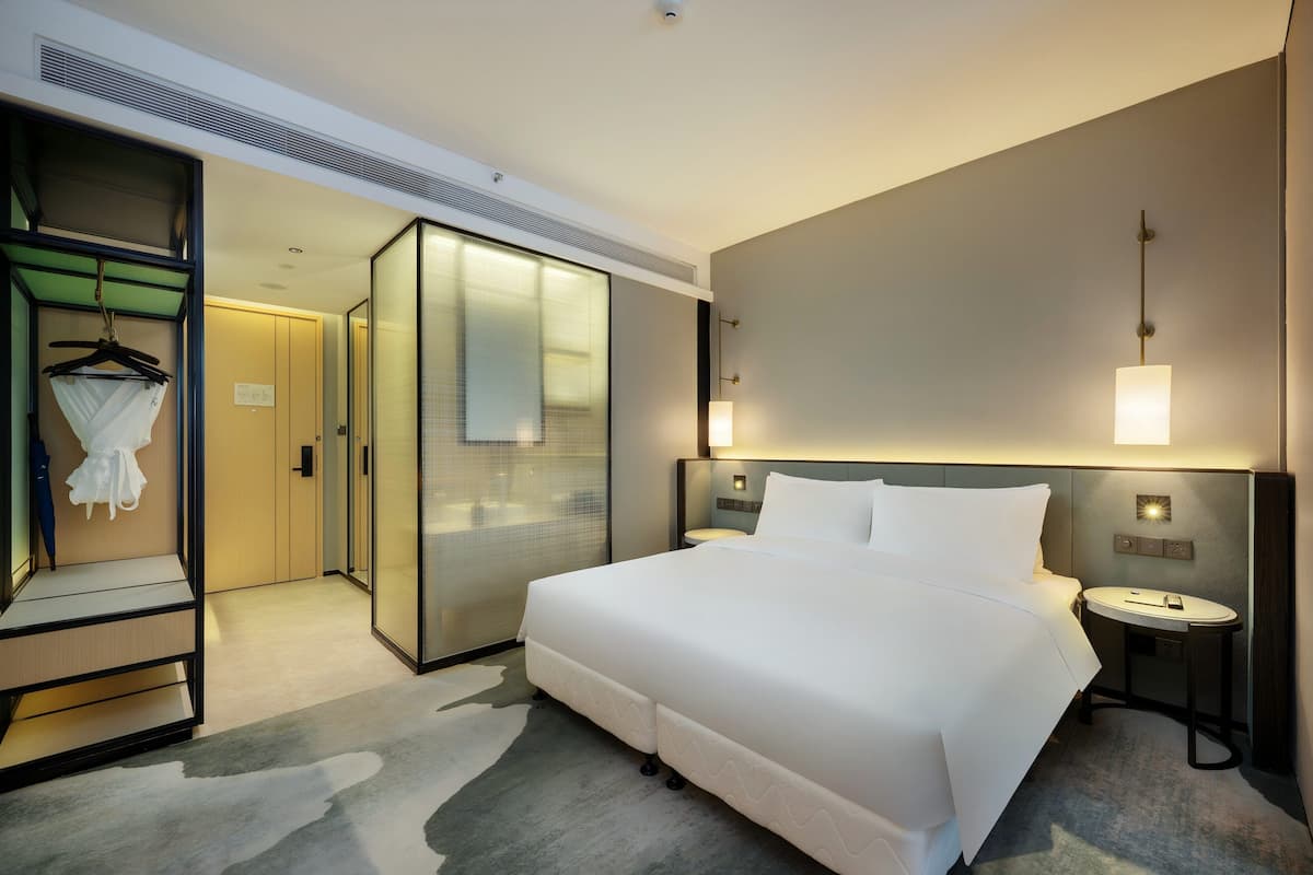 Quarto de hotel com uma cama grande, uma mesinha de cabeceira, roupão pendurado e um closet espaçoso.