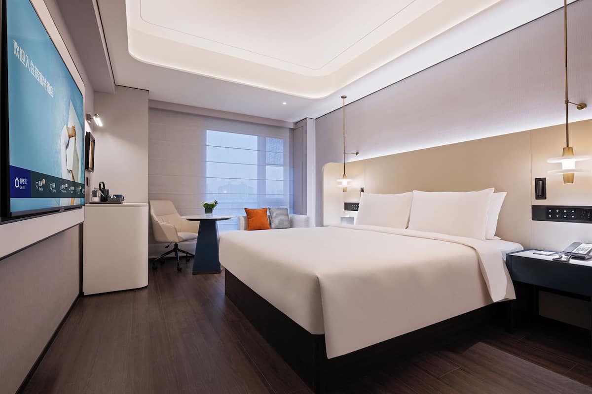 Quarto de hotel moderno com uma cama grande, uma escrivaninha, uma cadeira e uma televisão.