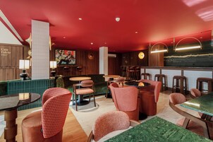 Interior de restaurante com paredes de madeira, teto vermelho e várias áreas de estar, incluindo mesas redondas e cadeiras acolchoadas.