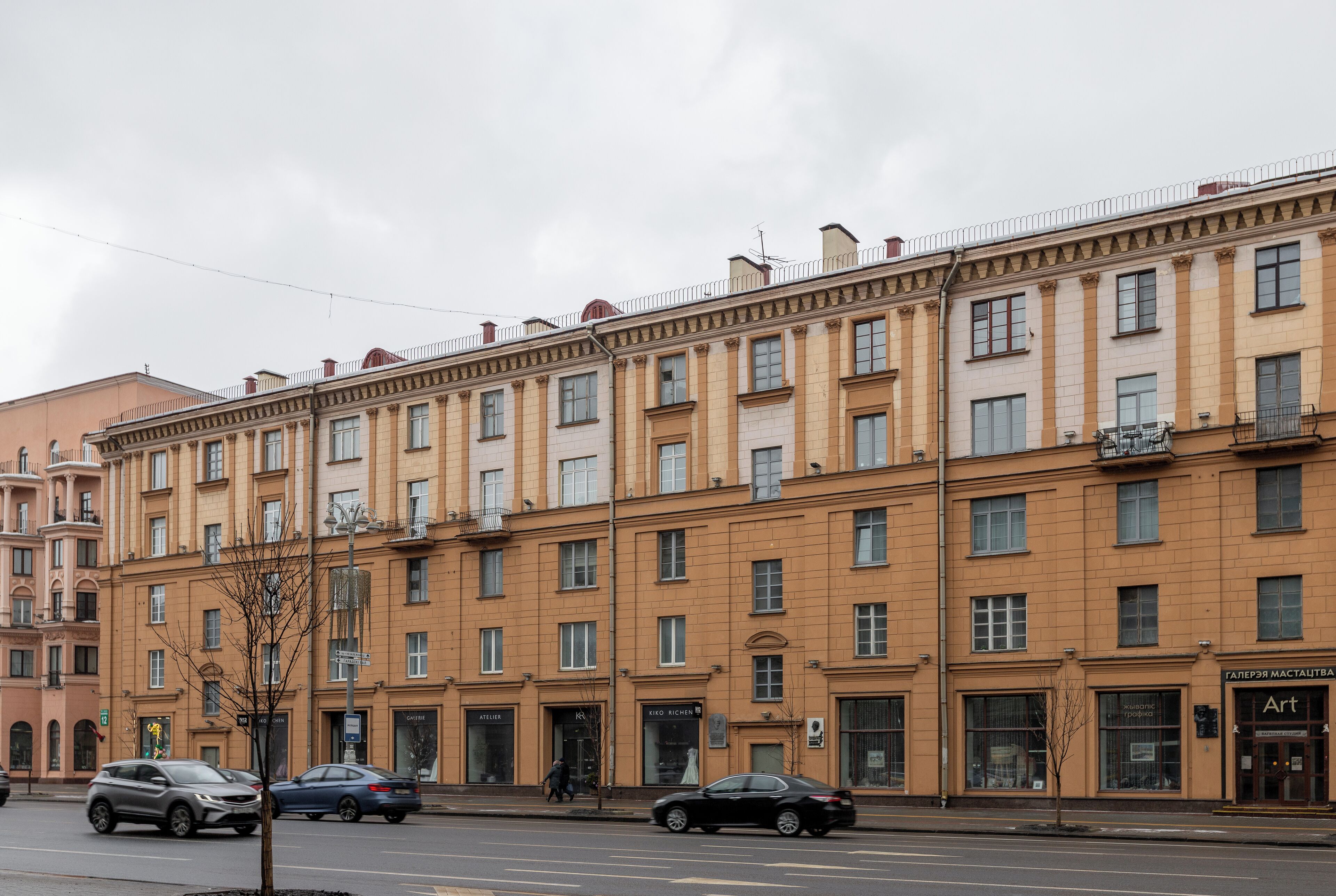 Uma fileira de edifícios com vários andares, com lojas no andar térreo e uma rua em frente.