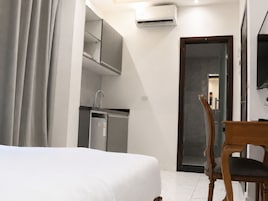 Quarto de hotel com cama, escrivaninha, cadeira, cozinha compacta e ar condicionado.