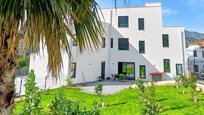 Um edifício moderno e branco, com várias janelas, um gramado bem cuidado e uma palmeira.