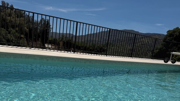 Piscina com água cristalina, pés de alguém e uma cerca ao fundo.