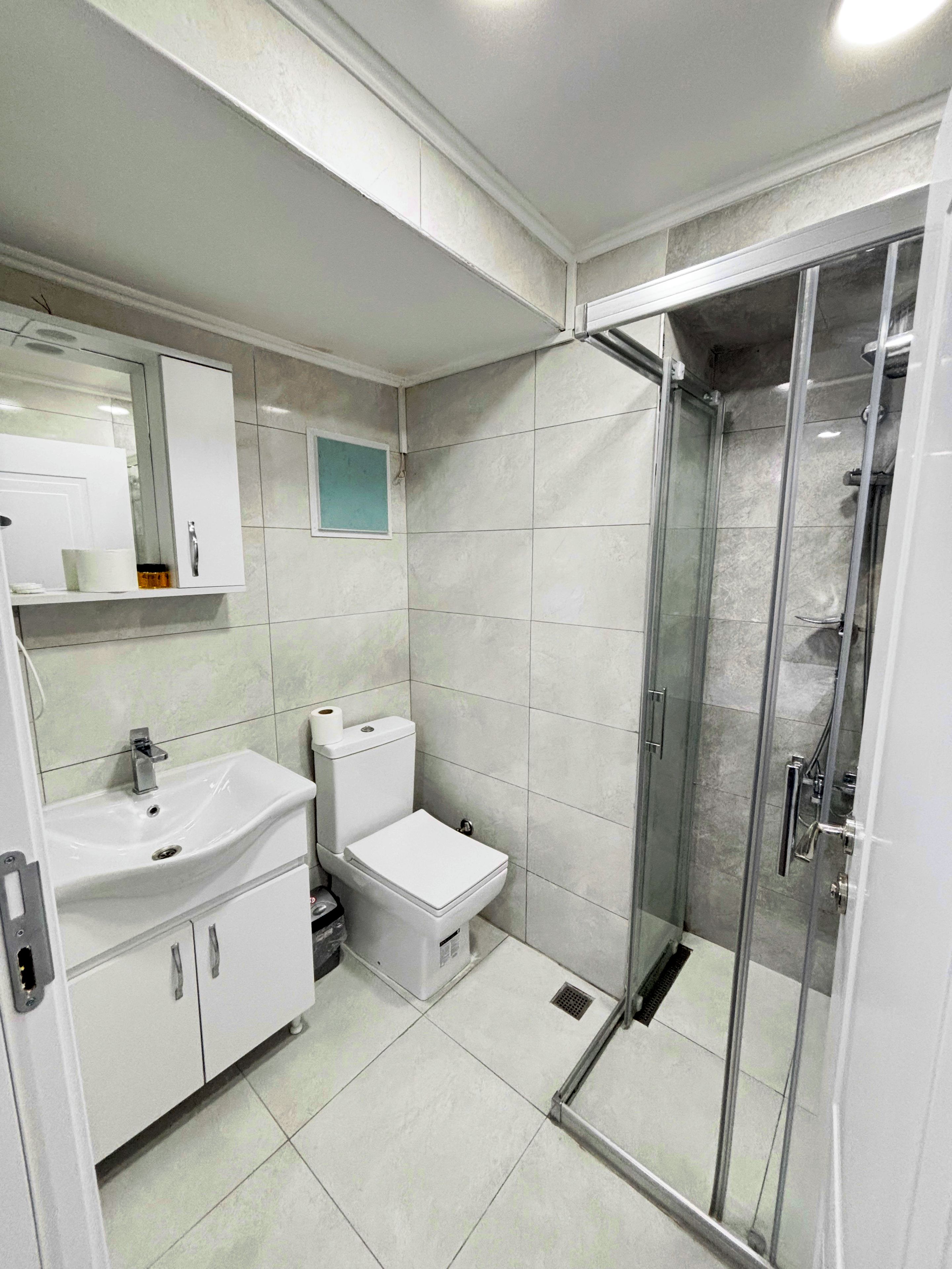 Uma casa de banho moderna com cabine de duche em vidro, uma sanita e uma pia branca.