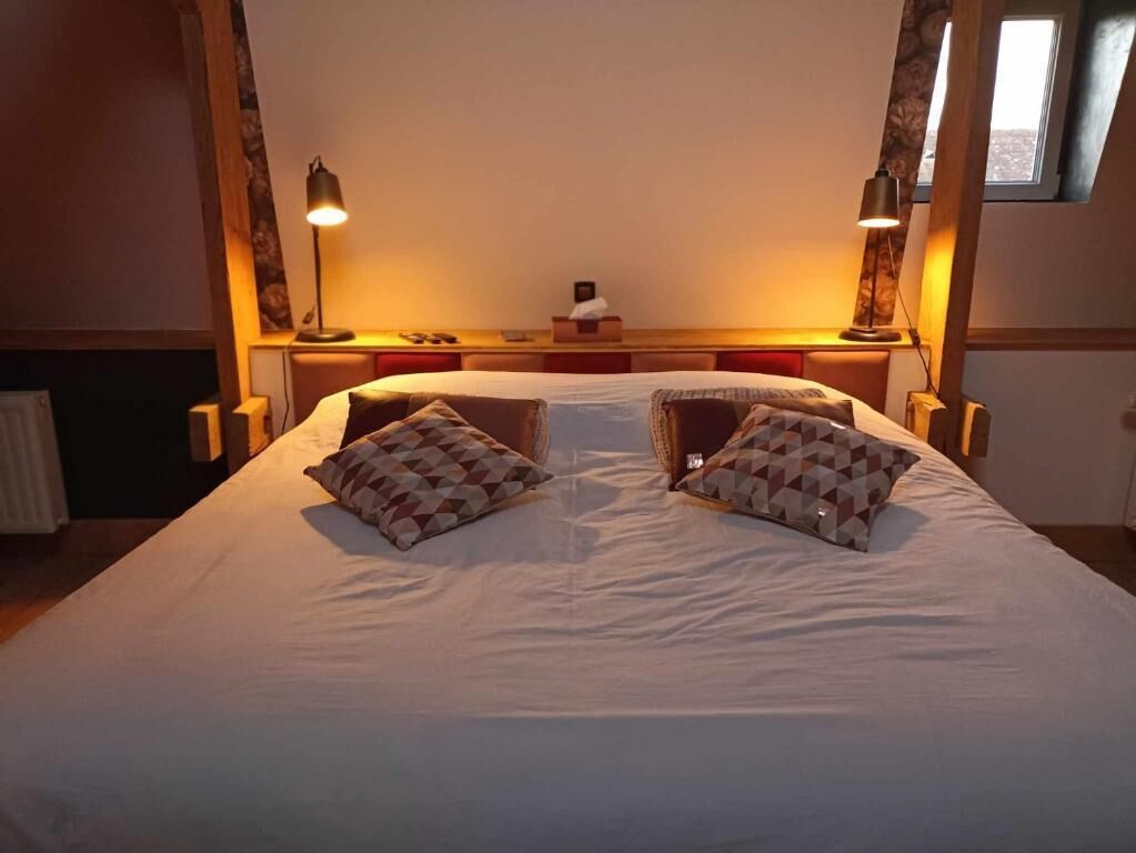 Uma cama grande com duas almofadas, abajures e uma janela com cortinas.