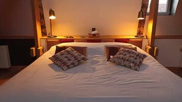 Uma cama grande com duas almofadas, abajures e uma janela com cortinas.