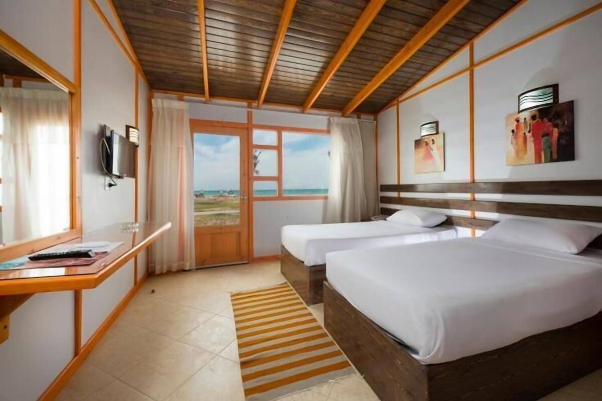 Quarto de hotel com duas camas, uma escrivaninha, uma televisão e janela com vista.