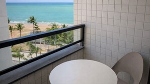 Uma varanda com piso de azulejos brancos, uma mesa redonda e duas cadeiras.