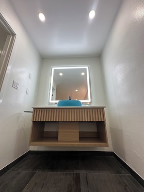 Casa de banho com toucador, espelho iluminado e chão escuro.