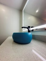 Uma casa de banho moderna com lavatório azul, espelho e luz no teto.