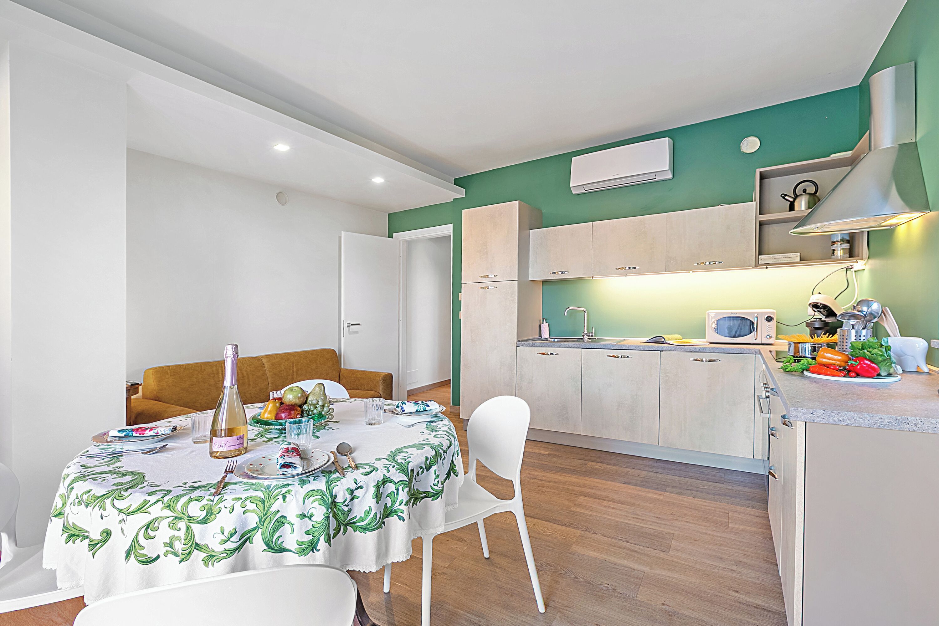 Uma cozinha moderna com armários brancos, micro-ondas e um espaço de refeições com uma mesa posta para dois.